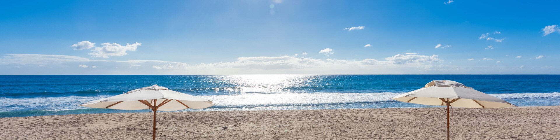 Uma praia com dois guarda-sóis e espreguiçadeiras voltadas para o oceano.