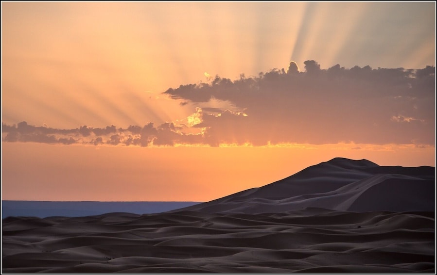 Paisagem desértica com dunas de areia e um pôr do sol.