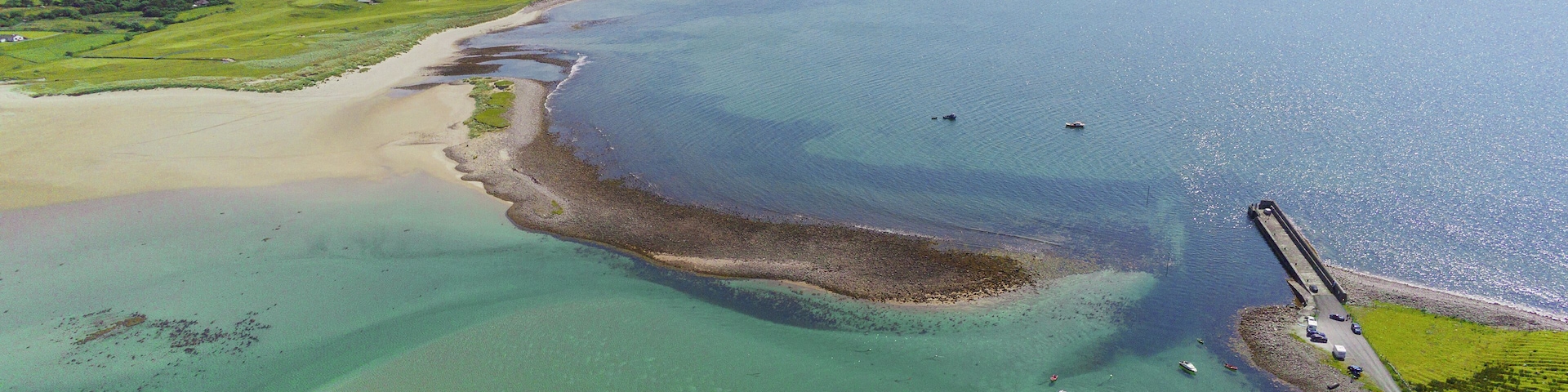 Paisagem costeira com uma praia arenosa, águas turquesa cristalinas e uma ponte ligando a terra.
