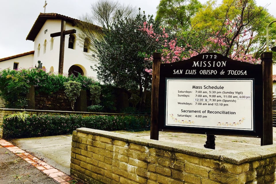 Um letreiro de igreja com o horário das missas e um aviso sobre o Sacramento da Reconciliação.