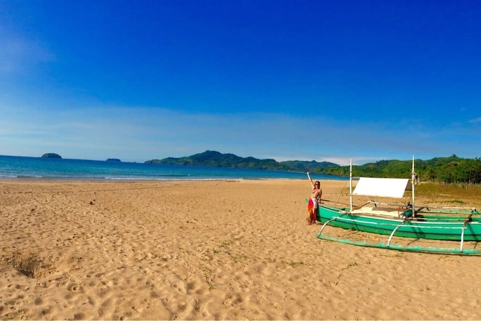 Uma praia arenosa com um barco verde e uma pessoa ao lado.