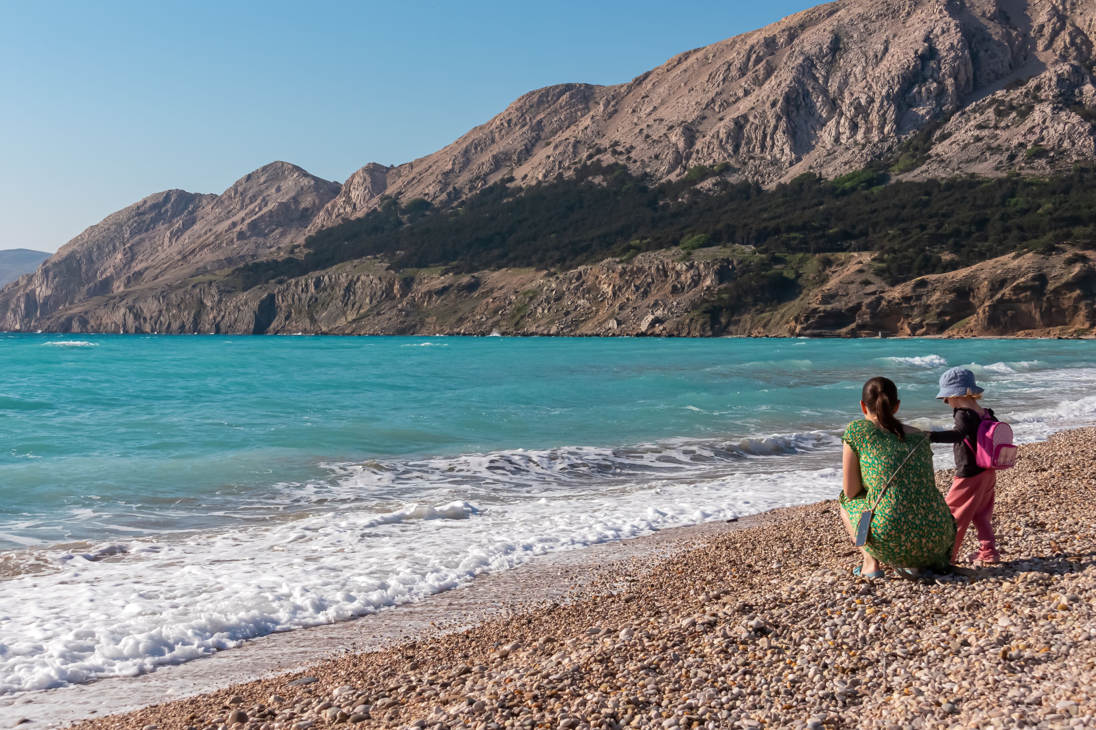Costa rochosa com águas turquesa translúcidas e montanhas ao fundo.