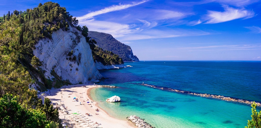 Paisagem costeira com uma praia de areia branca, águas turquesa cristalinas e um escarpe rochoso.