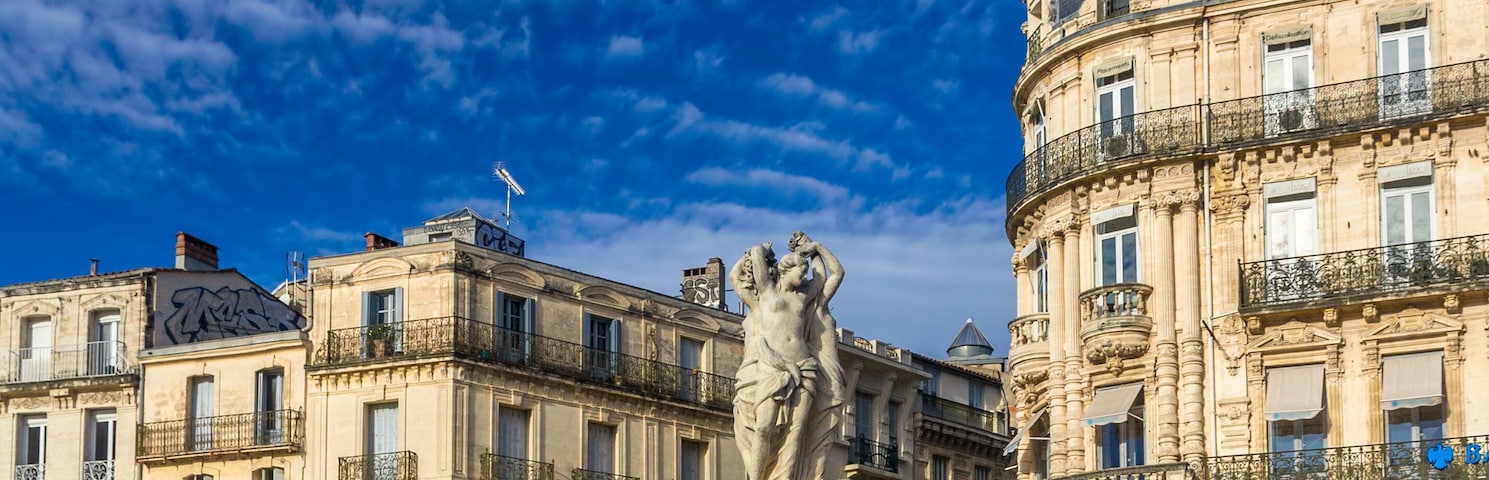 Uma fonte com uma estátua, rodeada por edifícios históricos com varandas e uma cúpula.