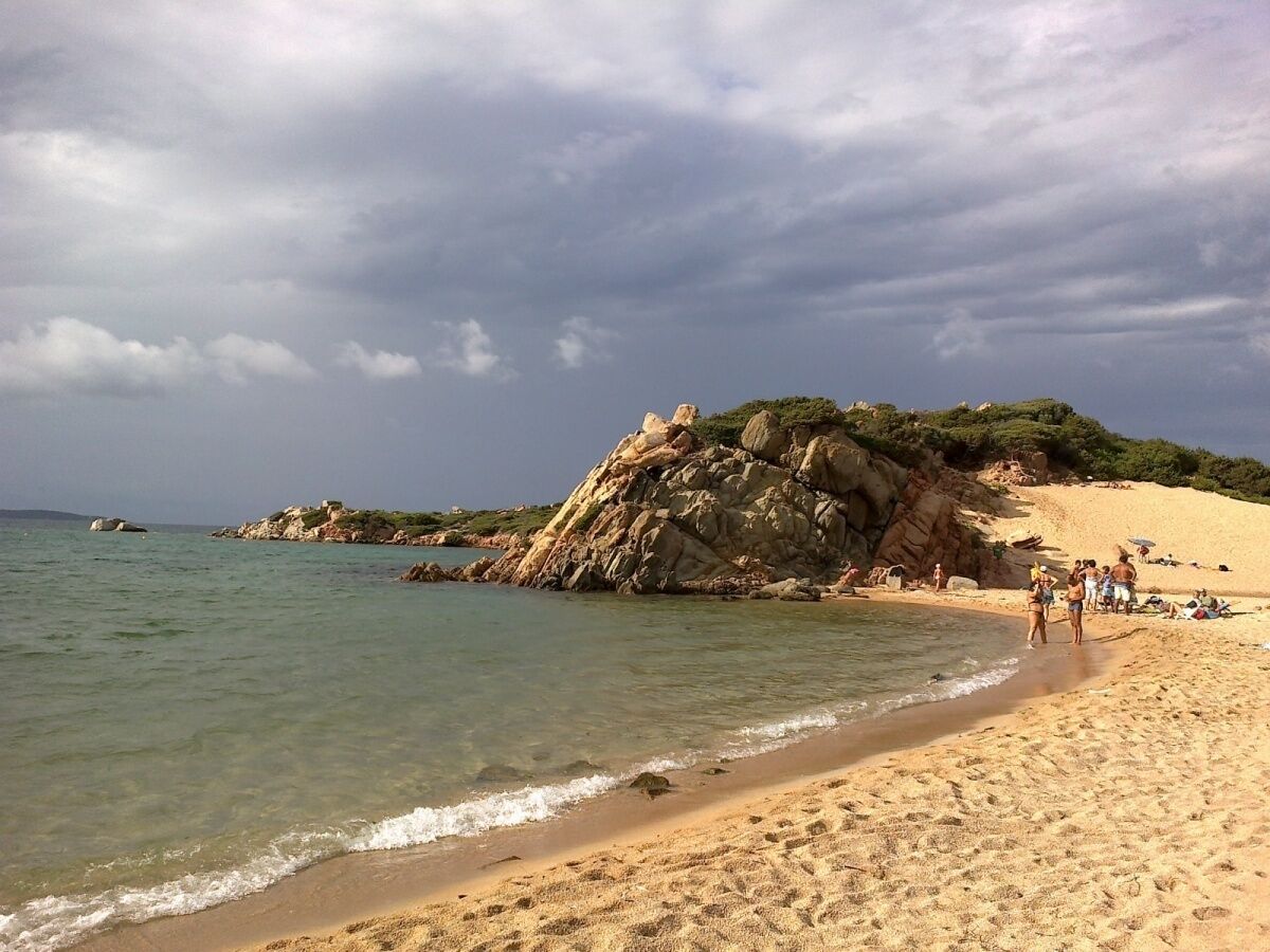 Uma praia com águas cristalinas, areal arenoso e falésias rochosas.