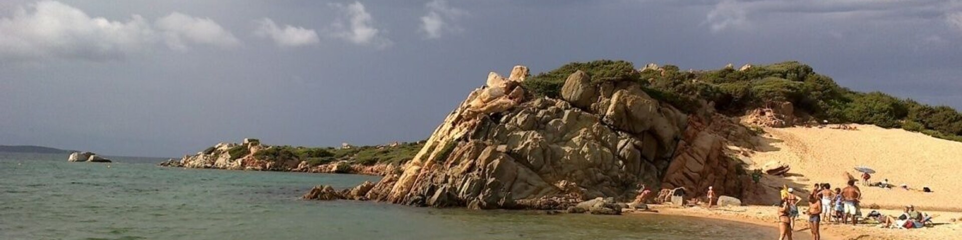 Uma praia com águas cristalinas, areal arenoso e falésias rochosas.