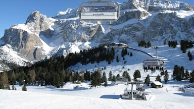 Um teleférico com montanhas ao fundo, encostas cobertas de neve e um céu azul límpido.