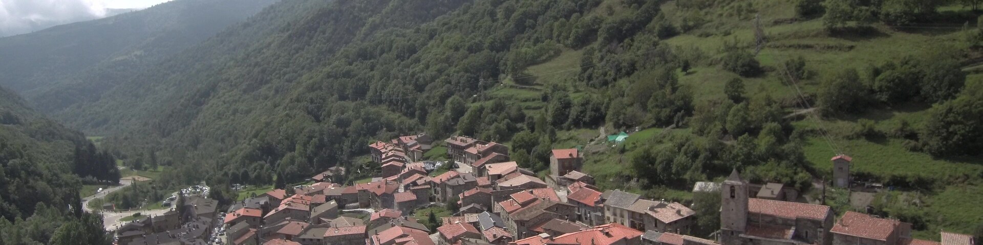 Uma aldeia montanhosa com edifícios de telhados vermelhos e uma estrada sinuosa.