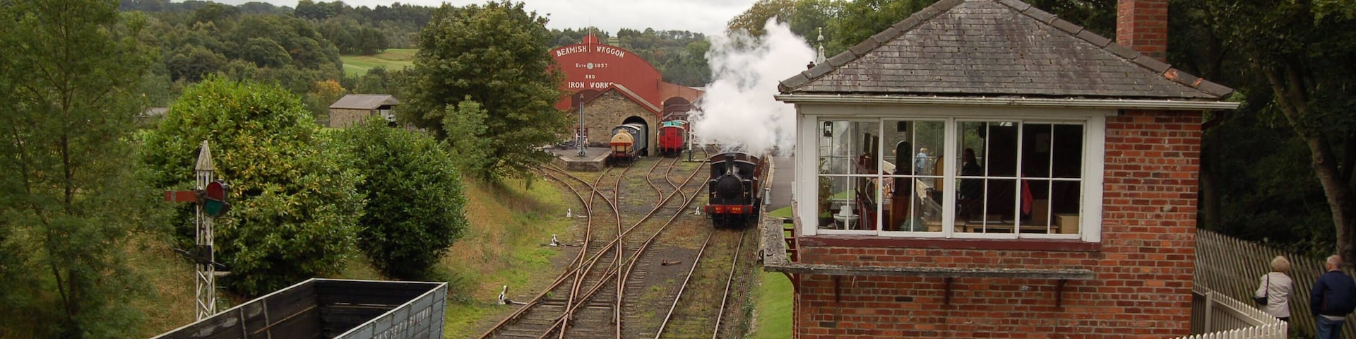 Beamish Museum, County Durham, England. The view west from the east footbridge on the Town railway, showing the signal box (obscuring the station, which has a train in the platform), with the goods shed platform & coal drop in the distance.