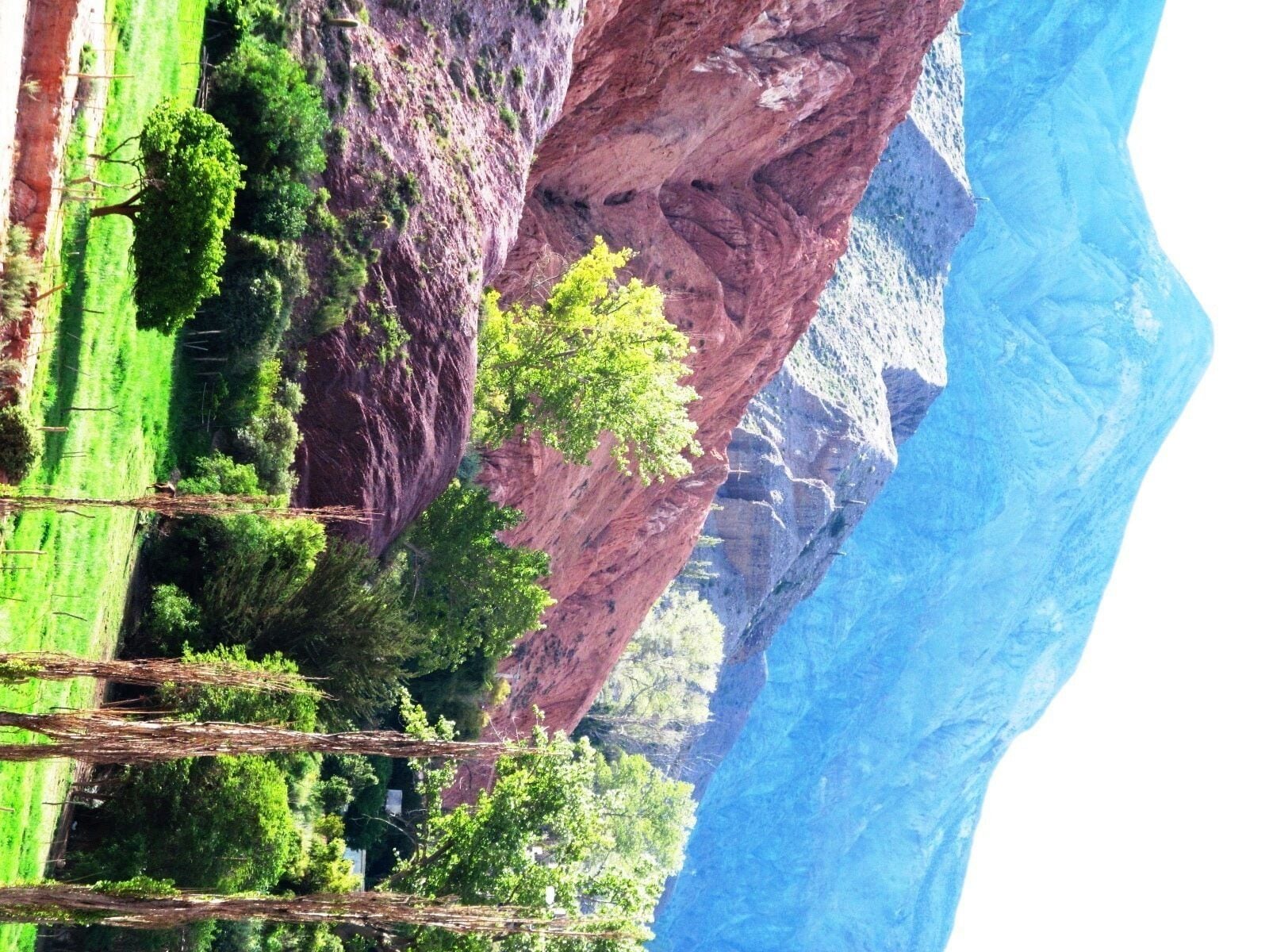 Um cânion com campos verdes e falésias de rocha avermelhada.