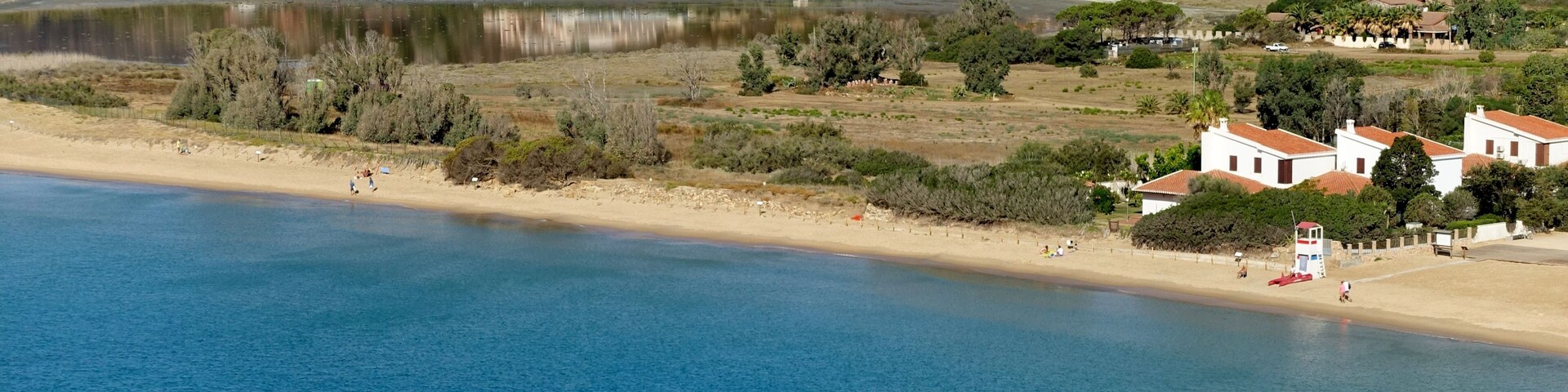 Uma cidade costeira com praia, lago e montanhas ao fundo.