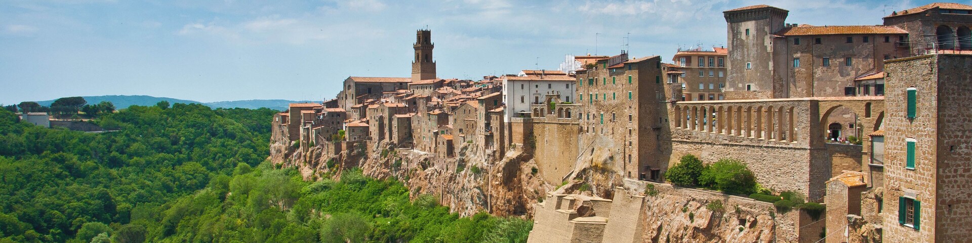 Uma cidade histórica empoleirada em um penhasco, com vegetação exuberante, edifícios de pedra e uma torre imponente.