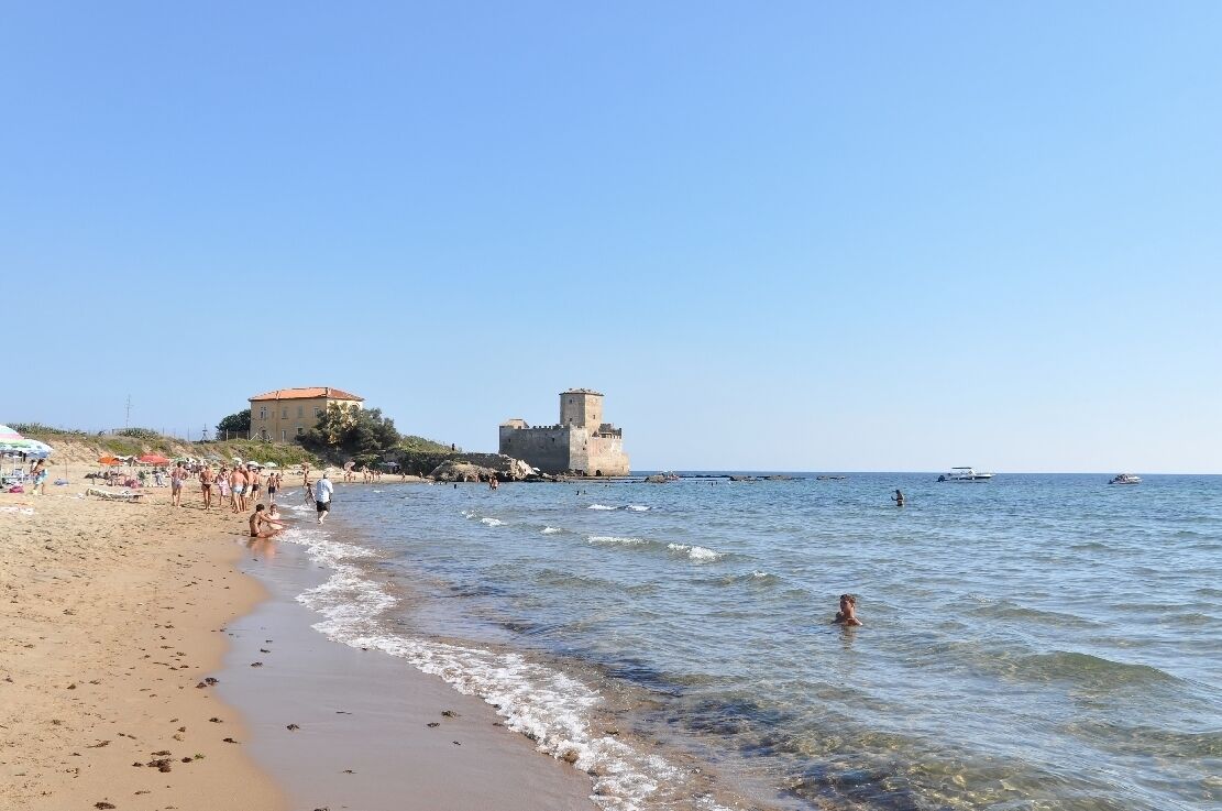 Uma praia com pessoas, um castelo e barcos.