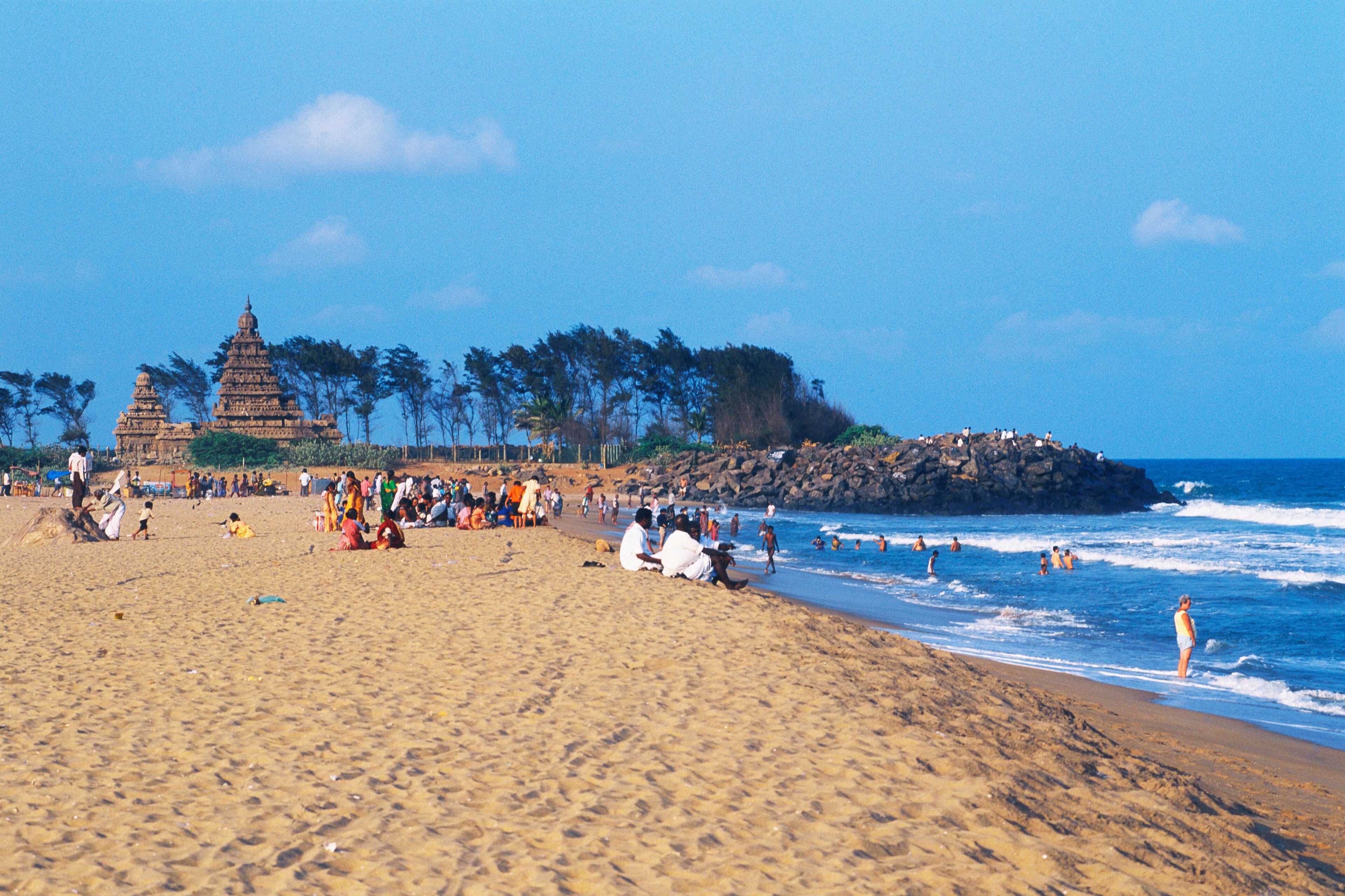 Uma praia com pessoas, um templo e um afloramento rochoso.