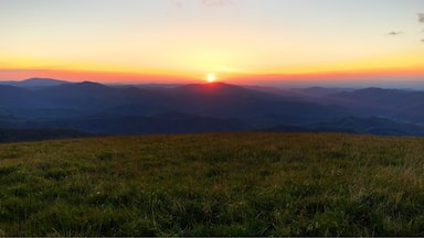 Um pôr do sol sobre uma cordilheira com um primeiro plano gramado.