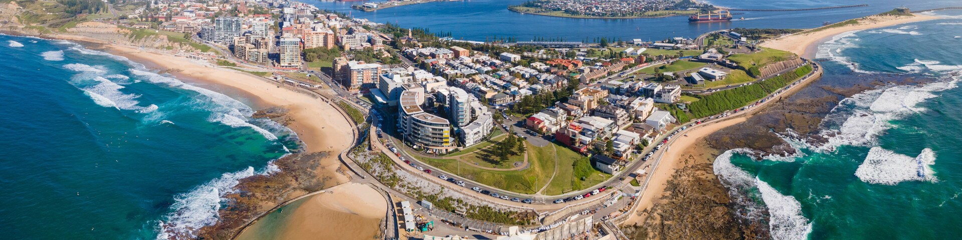 Vista aérea de uma cidade costeira com praia, edifícios residenciais e um porto.