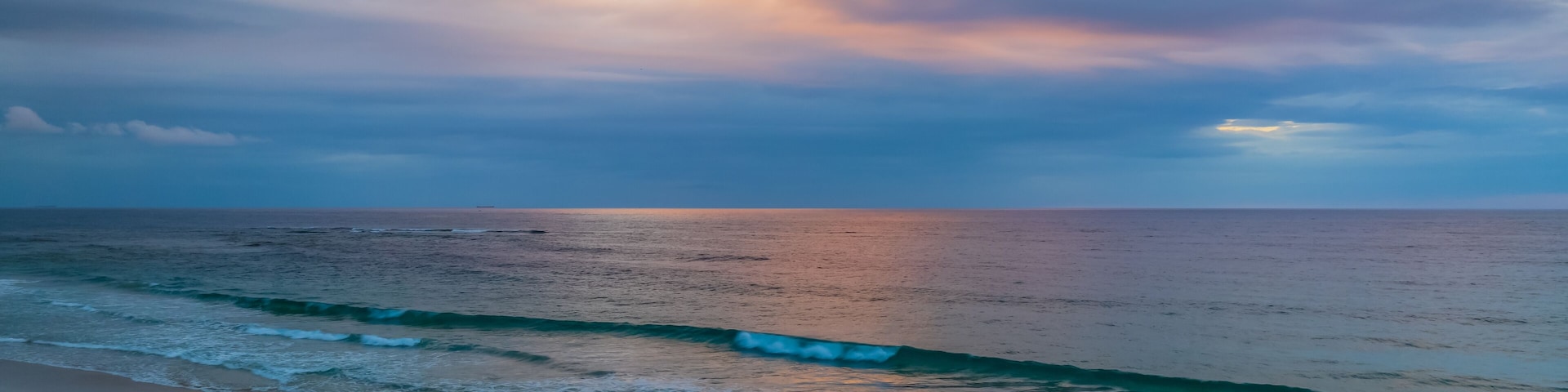 Uma praia com ondas e um céu ao pôr do sol.