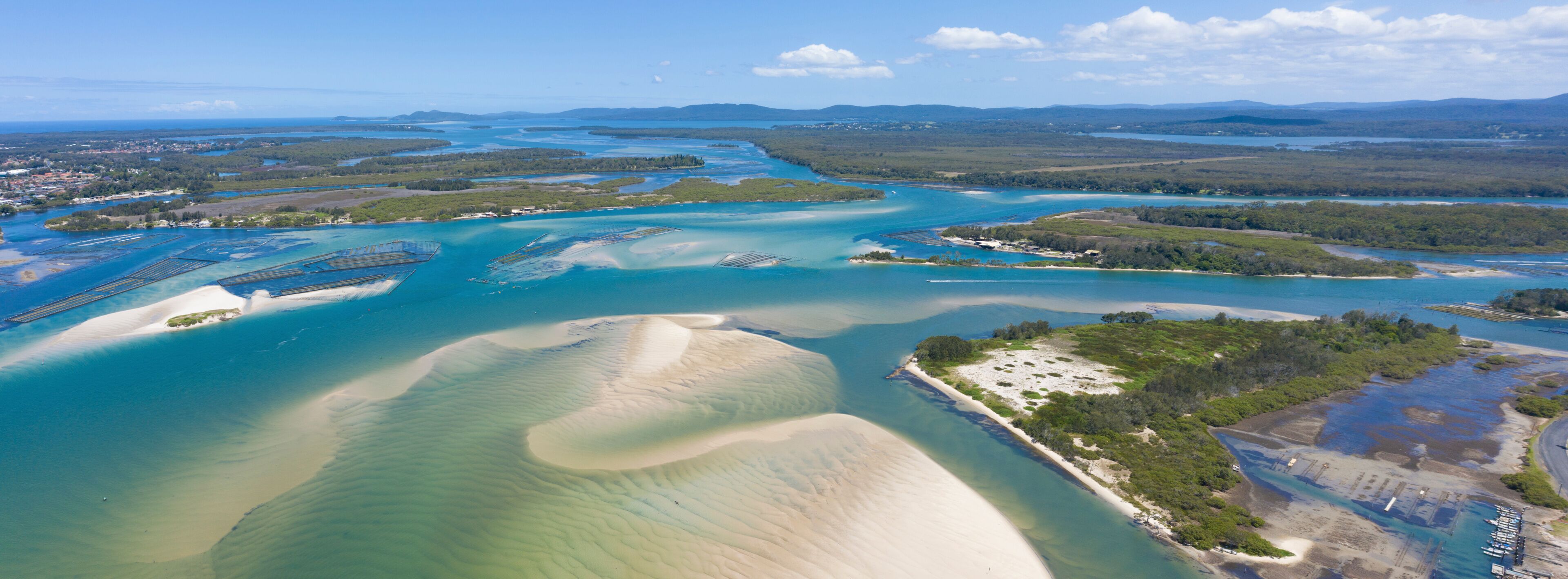 Vista aérea de uma área costeira com águas azul-claras, praias de areia e uma rede de canais.