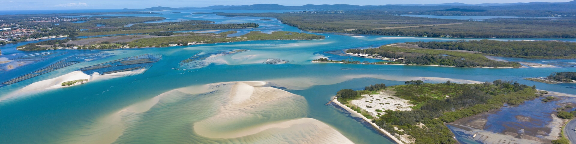 Vista aérea de uma área costeira com águas azul-claras, praias de areia e uma rede de canais.