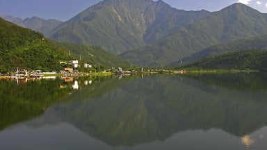Um lago tranquilo com uma cordilheira ao fundo e um pequeno povoado à esquerda.
