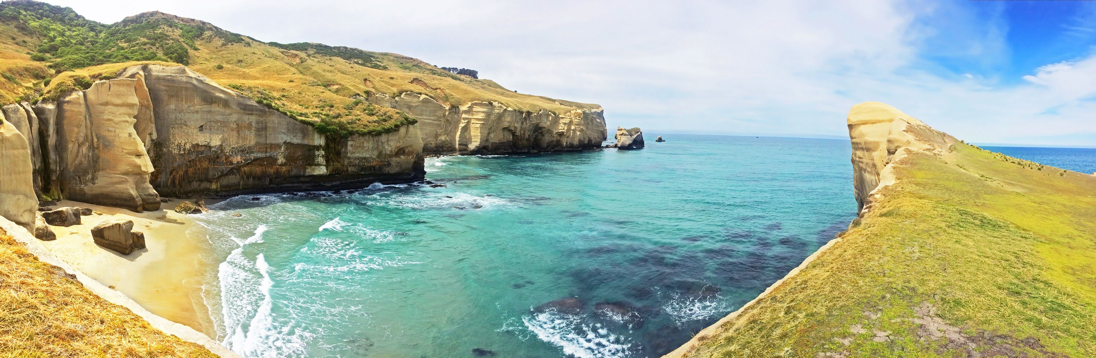 Paisagem costeira com falésias, uma praia e mar azul cristalino.