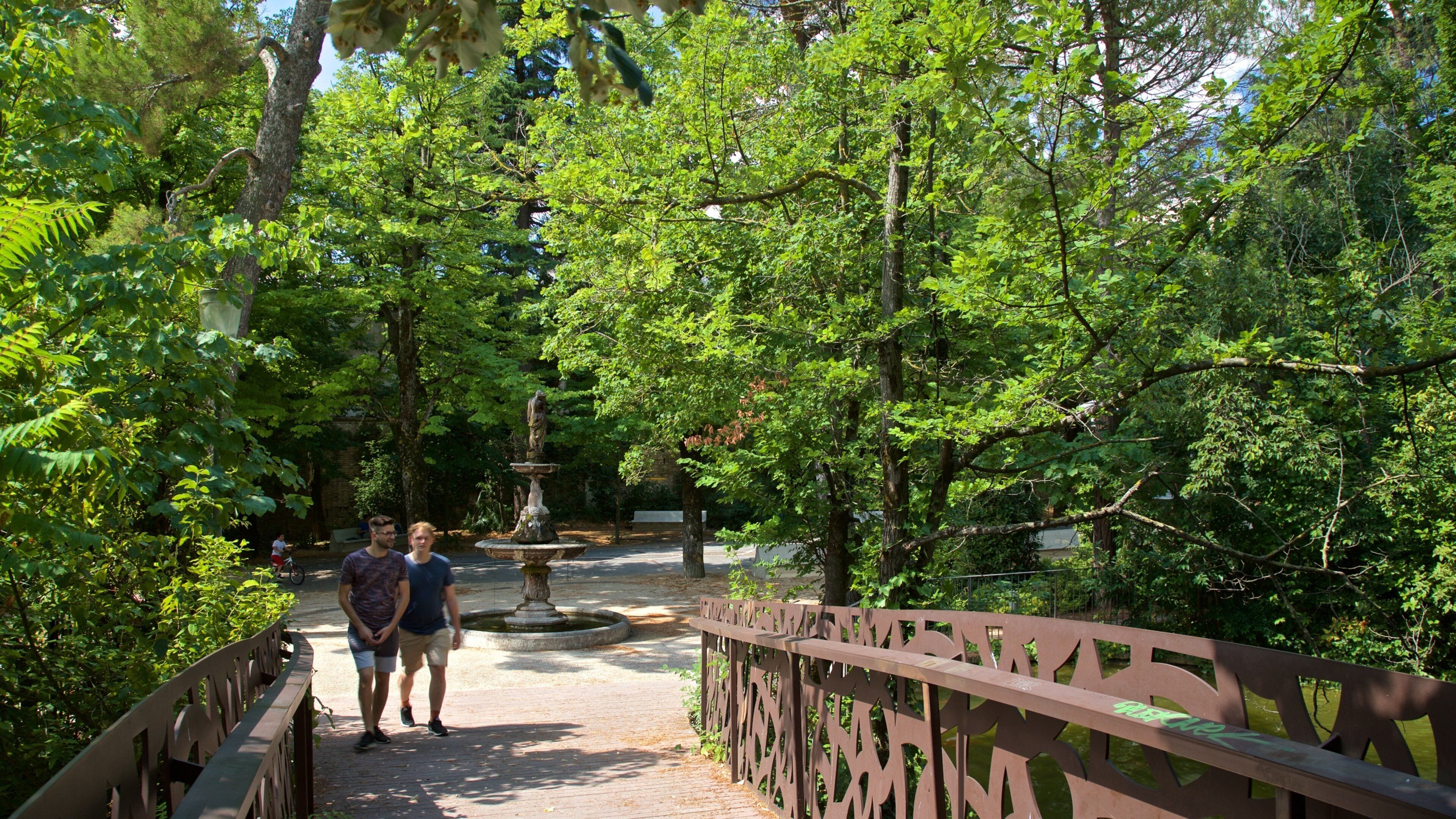 Um caminho com guarda-corpo de metal, rodeado por árvores verdes e uma estátua ao fundo.