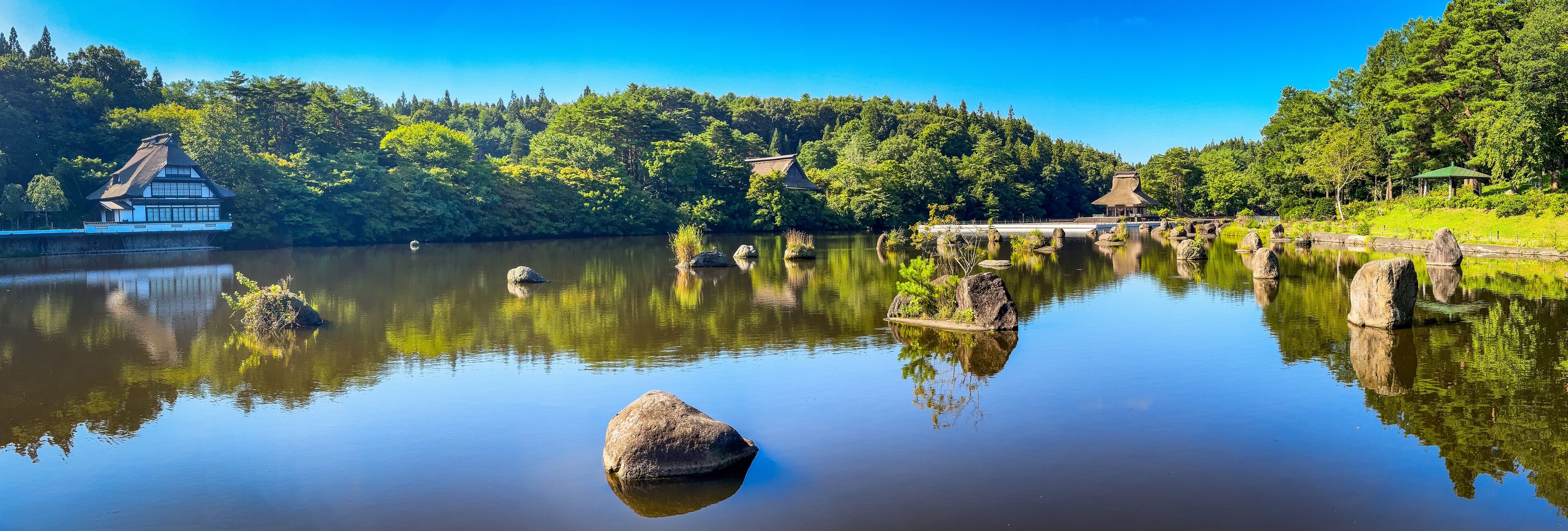 Um lago calmo refletindo árvores e arquitetura japonesa tradicional.
