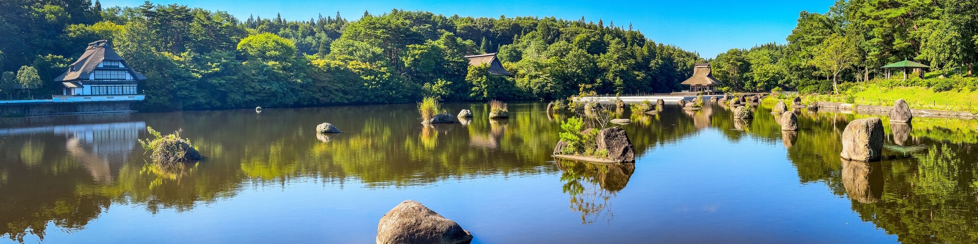 Um lago calmo refletindo árvores e arquitetura japonesa tradicional.