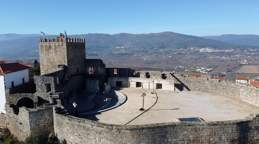 Uma fortaleza de pedra histórica com uma torre central, rodeada por muralhas e um pátio.