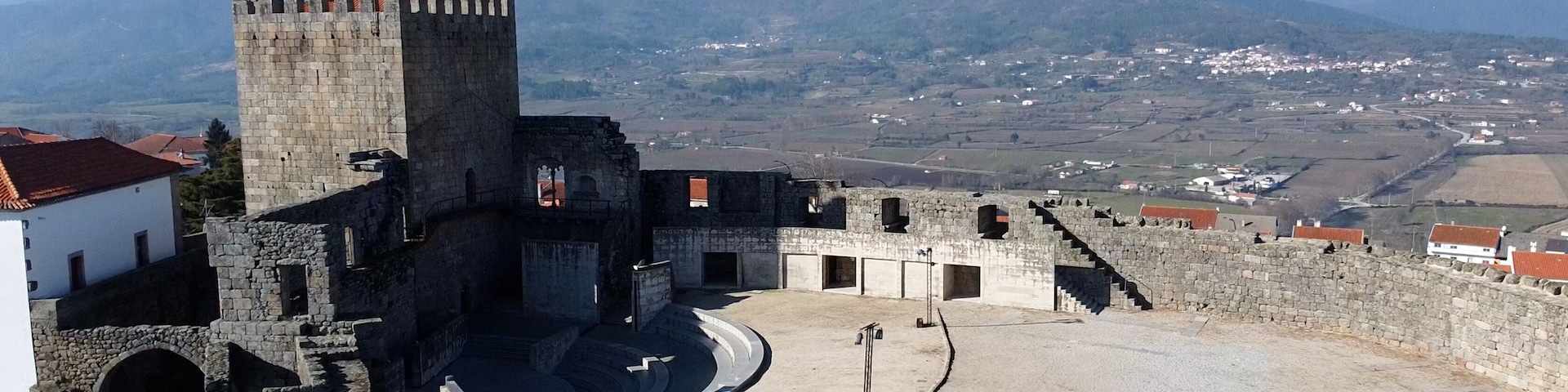 Uma fortaleza de pedra histórica com uma torre central, rodeada por muralhas e um pátio.