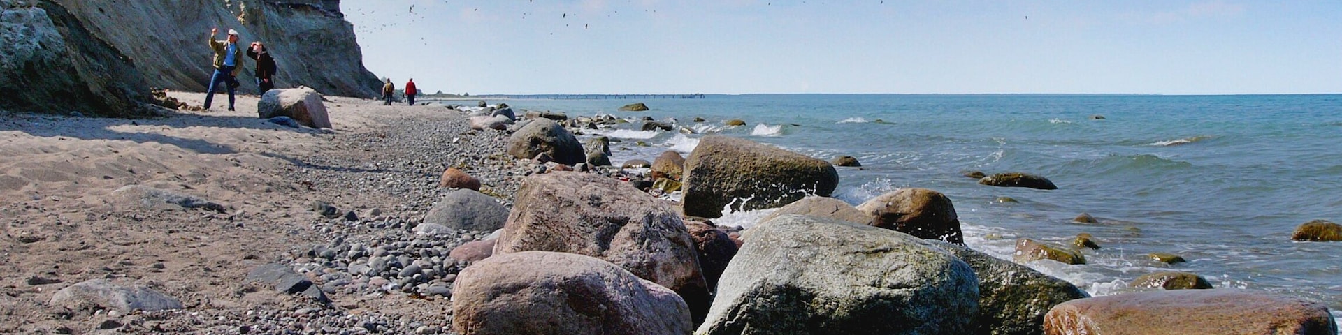 Uma praia rochosa com grandes pedras e um penhasco ao fundo.
