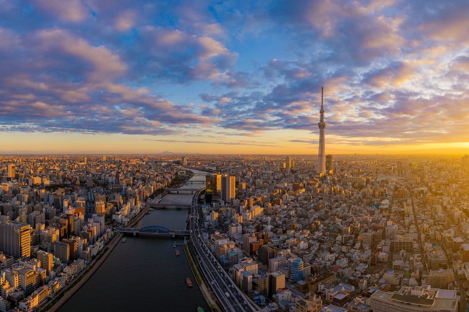 Paisagem urbana ao pôr do sol, com um rio serpenteando pela cidade e uma ponte ligando as margens.