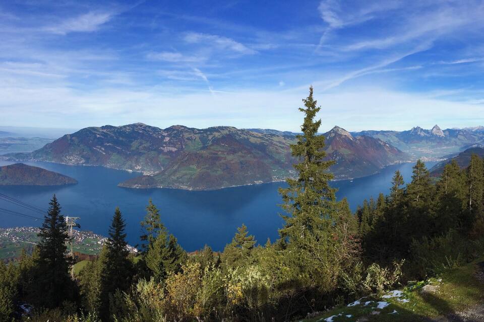 Paisagem montanhosa com um lago, florestas densas e uma cidade ao longe.