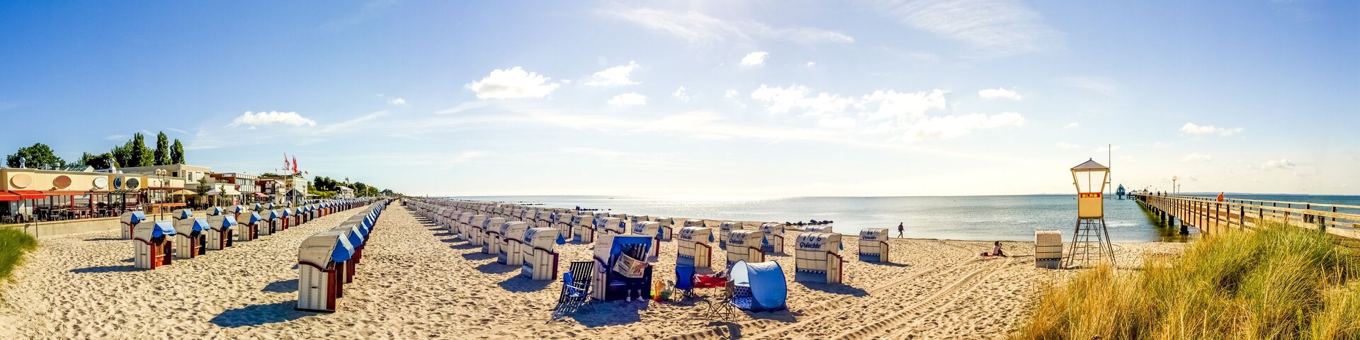 Uma praia com fileiras de cabanas, um píer e uma torre salva-vidas.