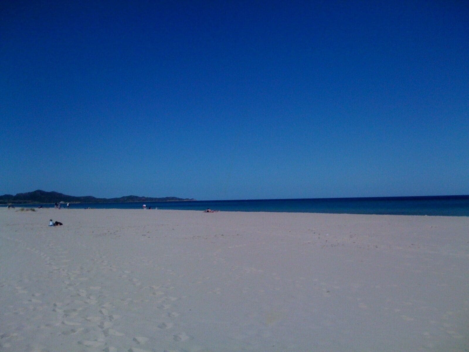 Uma extensa praia de areia com céu azul límpido e mar calmo.
