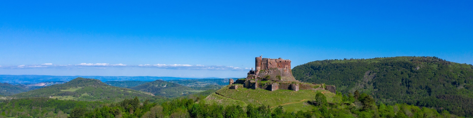 Um castelo histórico numa colina, rodeado por vegetação e sob um céu azul límpido.