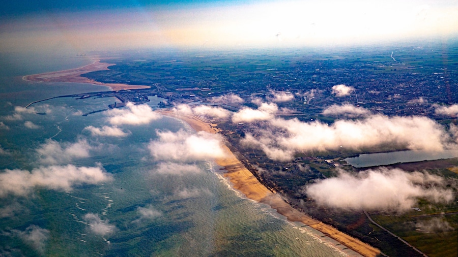 Vista aérea de uma área costeira com praia, rio e campos ao redor.