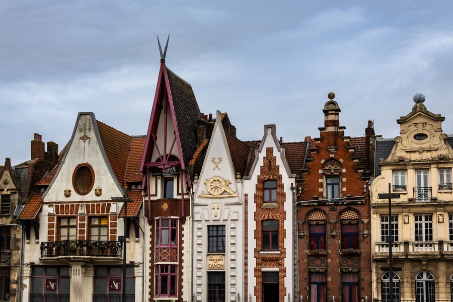 Uma fileira de edifícios históricos europeus com diferentes estilos arquitetônicos, incluindo telhados pontiagudos e fachadas decorativas.