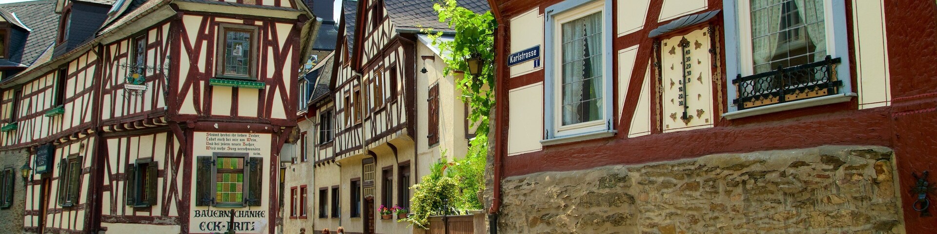 Rua com casas tradicionais em enxaimel, um muro de pedra e uma placa em alemão.