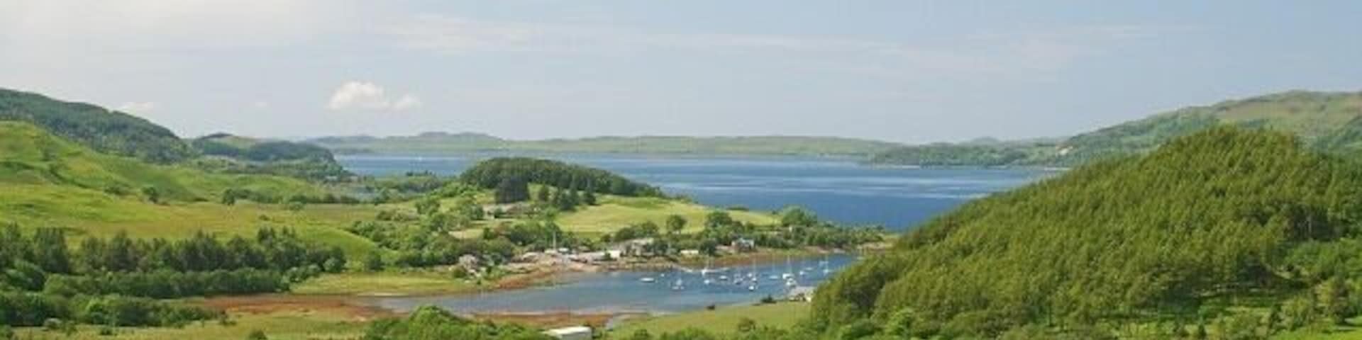 Paisagem costeira com colinas ondulantes, um lago e uma pequena aldeia.