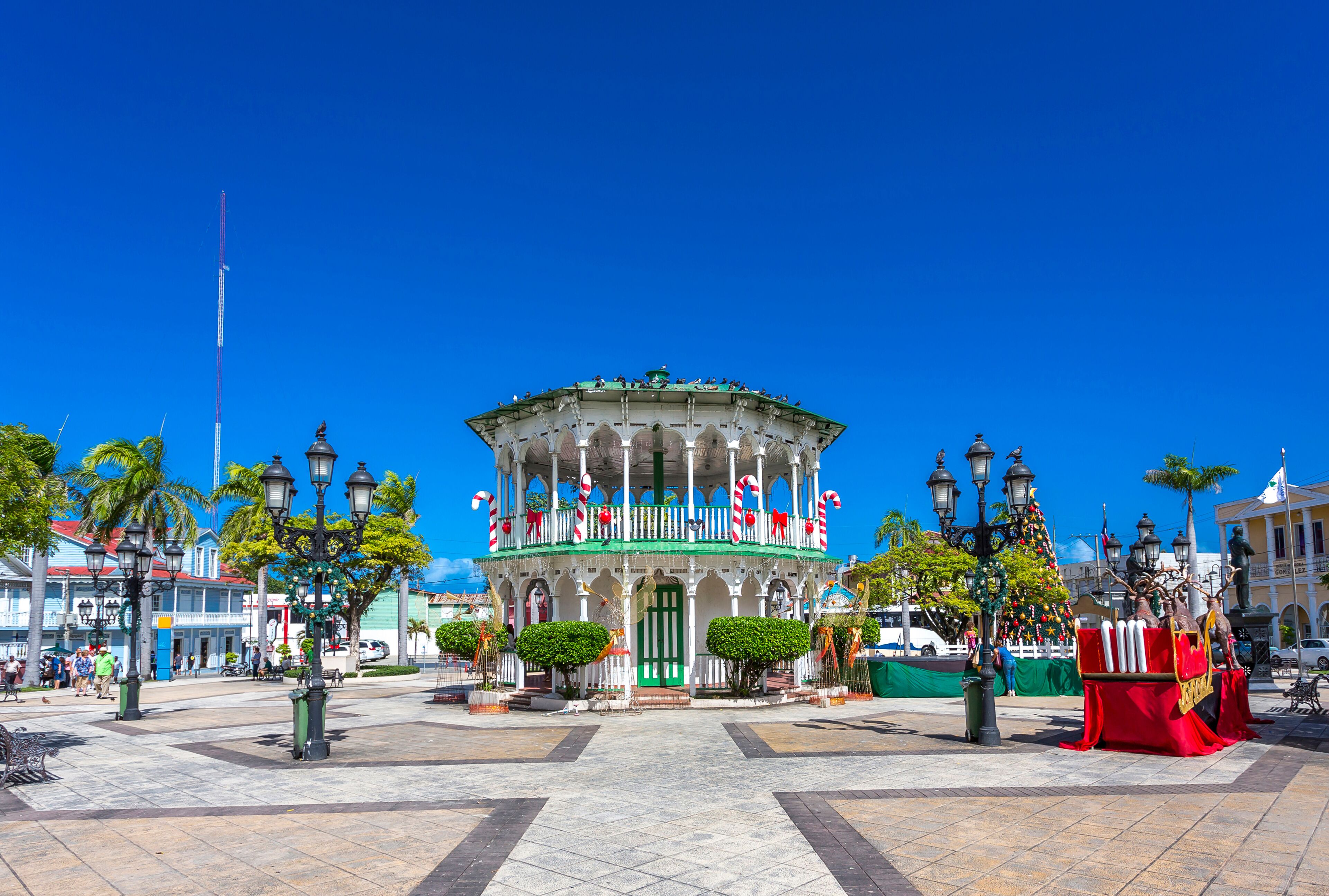 Um gazebo com decorações de cana de açúcar, cercado por uma praça com palmeiras e um pinheiro de Natal.