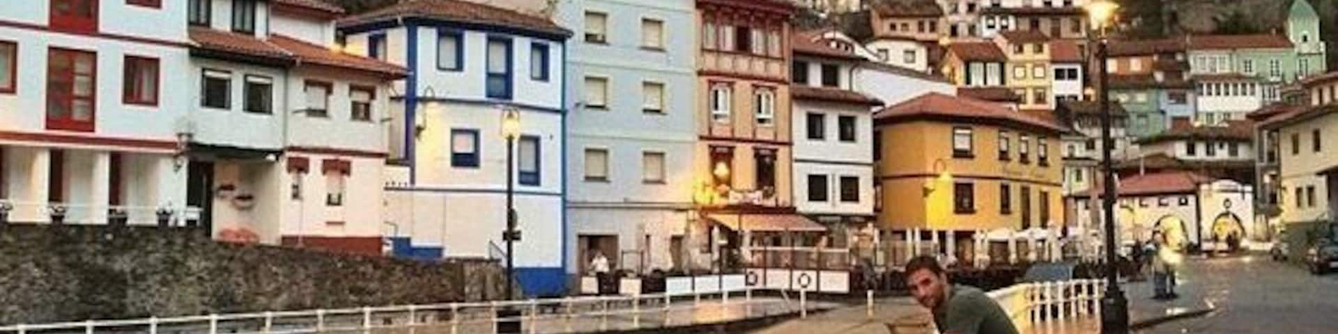 Uma cidade costeira com edifícios coloridos, um calçadão à beira-mar e uma pessoa apoiada na balaustrada.