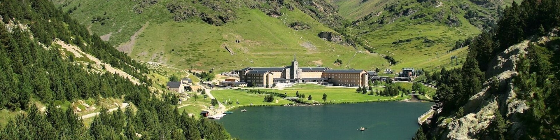 Paisagem montanhosa com um lago, uma ponte e um conjunto de edifícios.