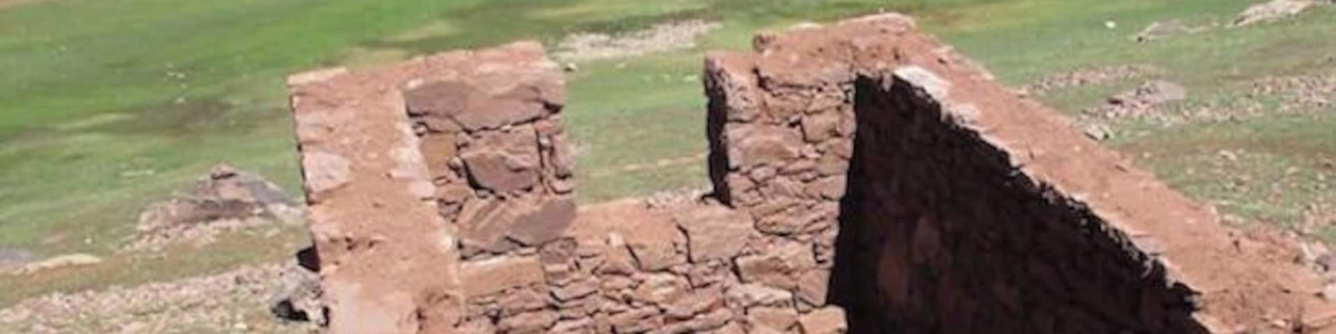 Ruínas antigas com muros de pedra e um campo gramado ao fundo.