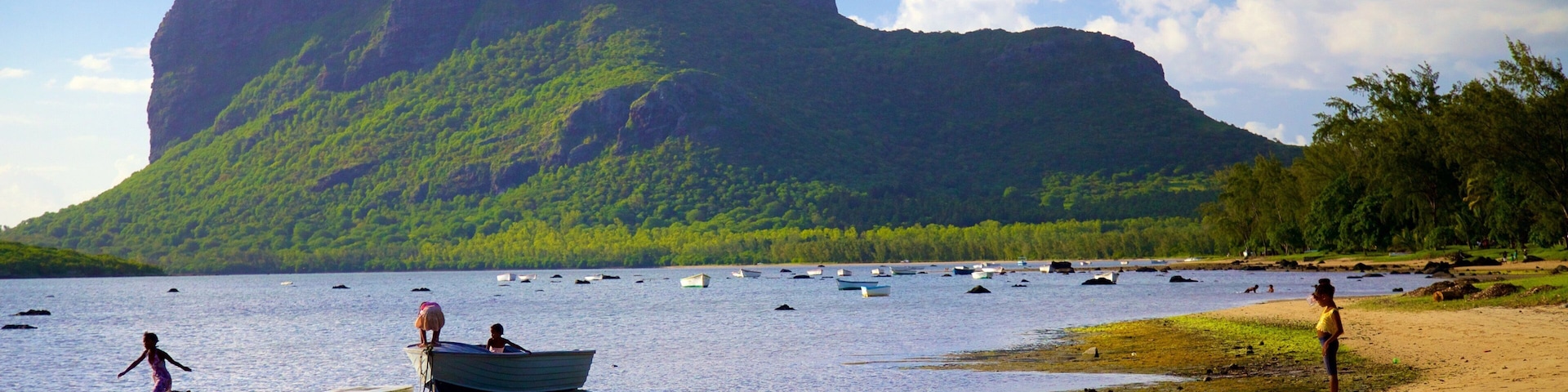 Uma praia com barcos, uma montanha imponente e pessoas.