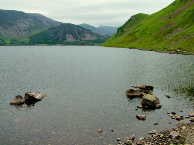 Um lago calmo rodeado por colinas verdes e margens rochosas.