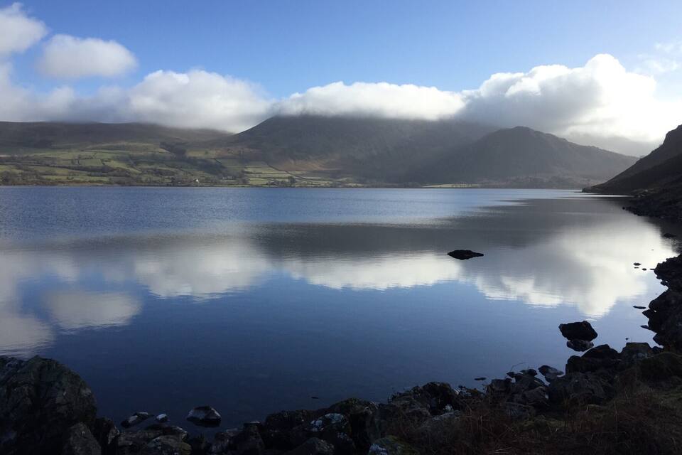 Um lago calmo rodeado por montanhas e um céu limpo.
