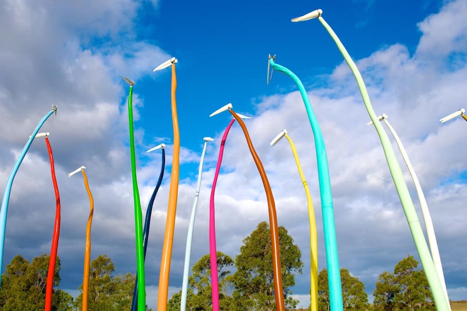 Uma fileira de turbinas eólicas coloridas contra um céu parcialmente nublado.