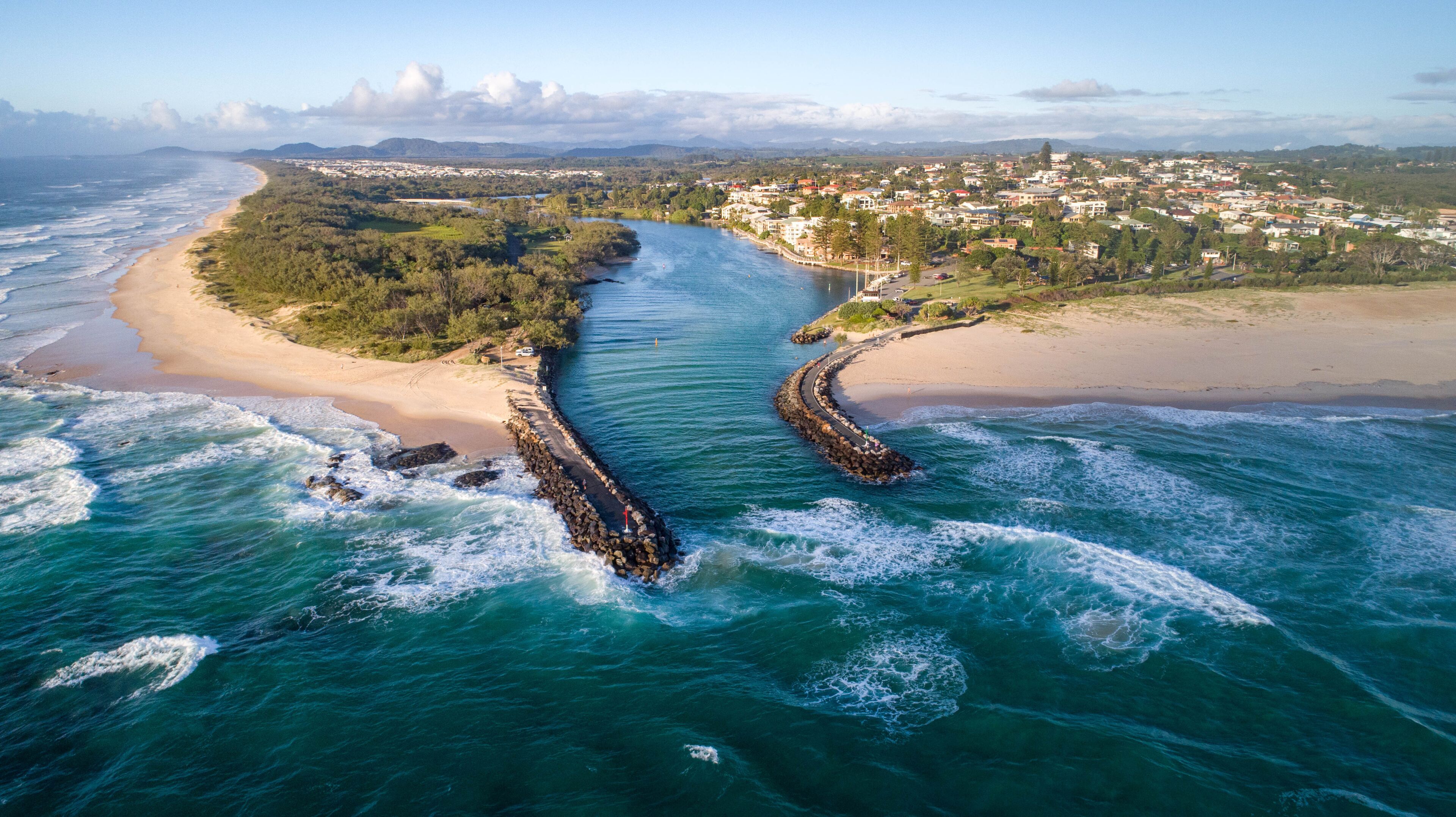 Uma vila costeira com uma estrada sinuosa, praias de areia e um molhe rochoso.