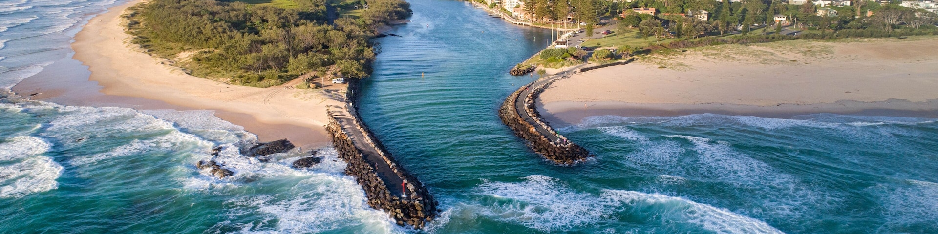 Uma vila costeira com uma estrada sinuosa, praias de areia e um molhe rochoso.
